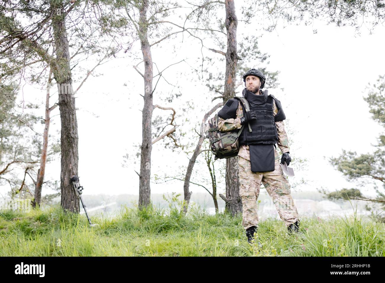 Young soldier in uniforms and tactical vest works in the forest and ...