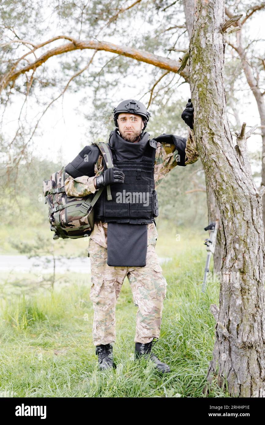 Young soldier in uniforms and tactical vest works in the forest and ...