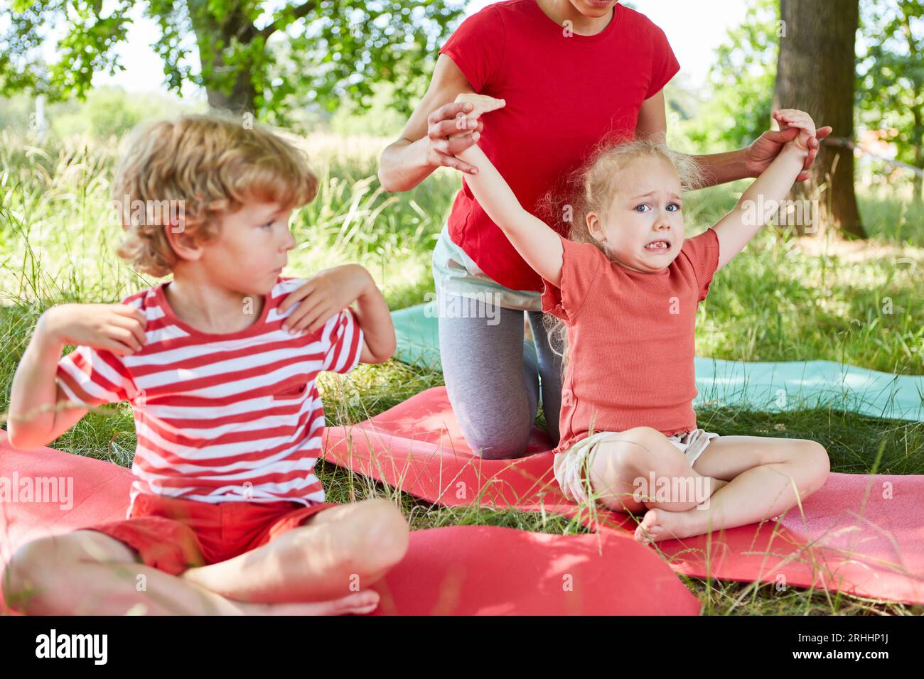 Mother Helping Daughter While Doing Exercise With Brother At Park Stock