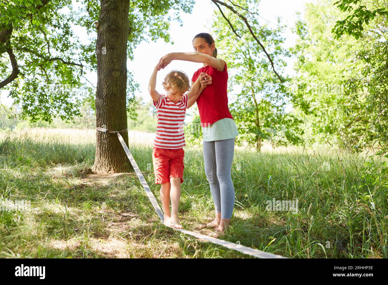 Mother supporting son doing slacklining in garden Stock Photo - Alamy