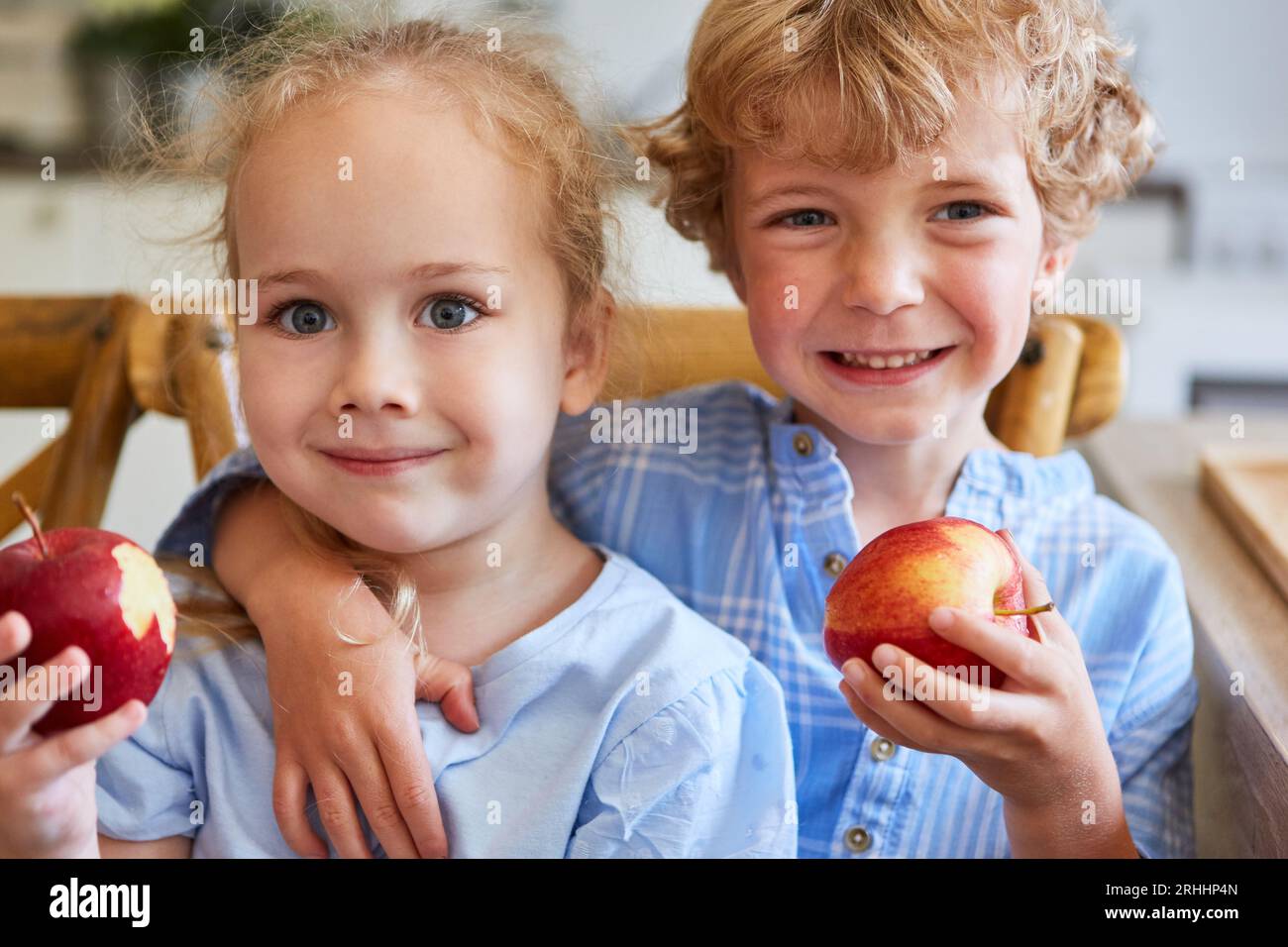 Smiling cute boy with arm around sister eating apple at home Stock ...