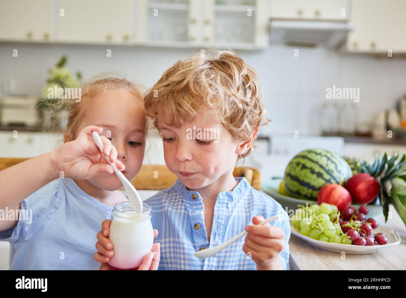 Girl eating parfait using spoon with brother while sitting by fruit on ...