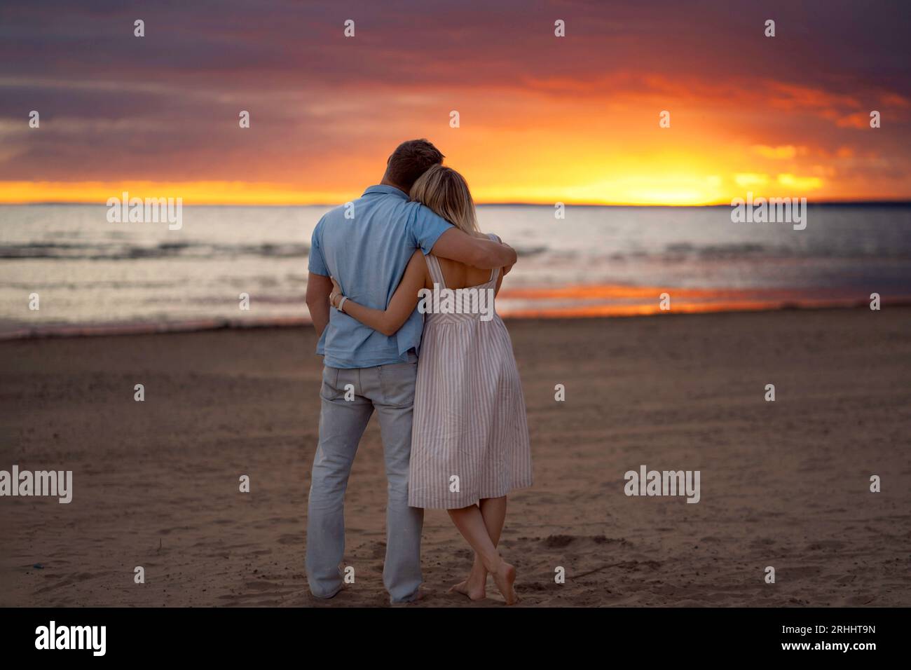 Happy couple standing on the beach at sunset hugging and looking at the ...