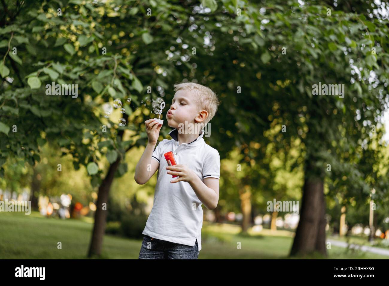 cute caucasian blond boy blowing soap bubbles in park. High quality ...
