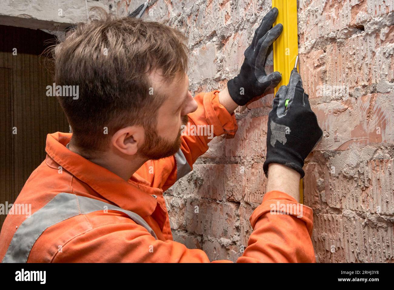 Young construction worker drawing a vertical line on a brick wall using ...