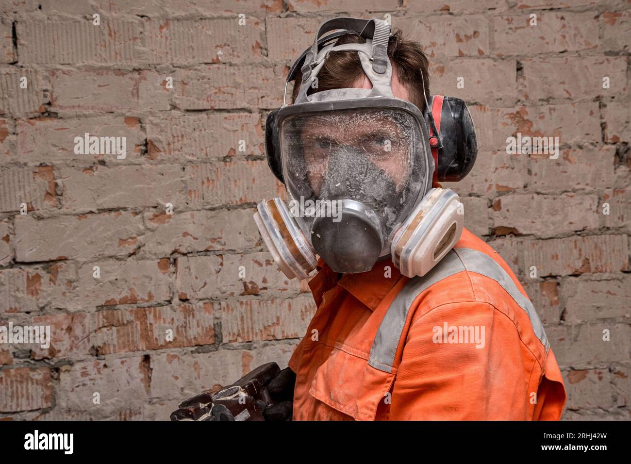 Builder wearing full face respirator mask and ear defenders for working in dusty and noisy ...