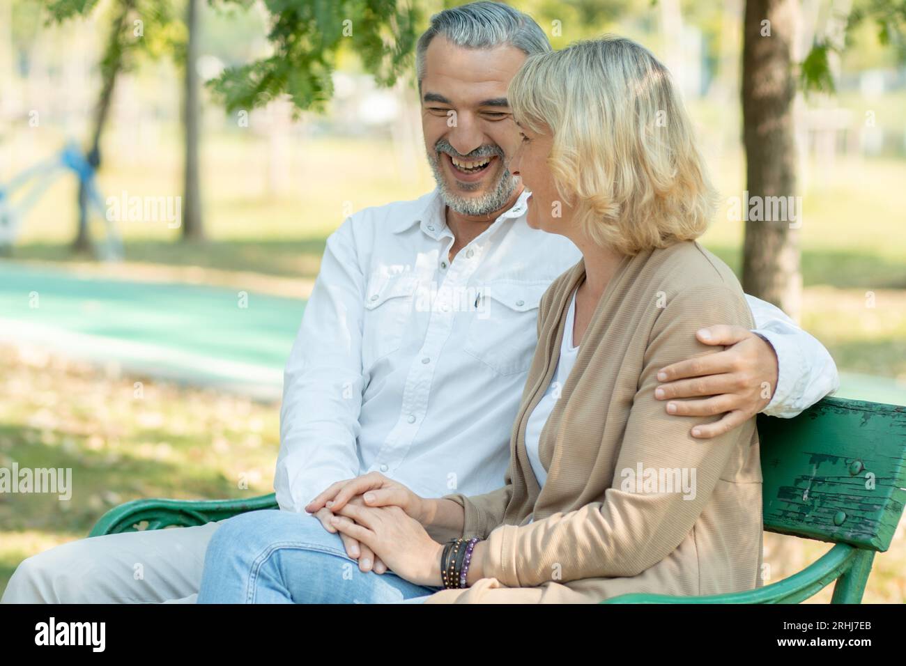 Happy elder love couple huge and smiling in romance sitting in park ...