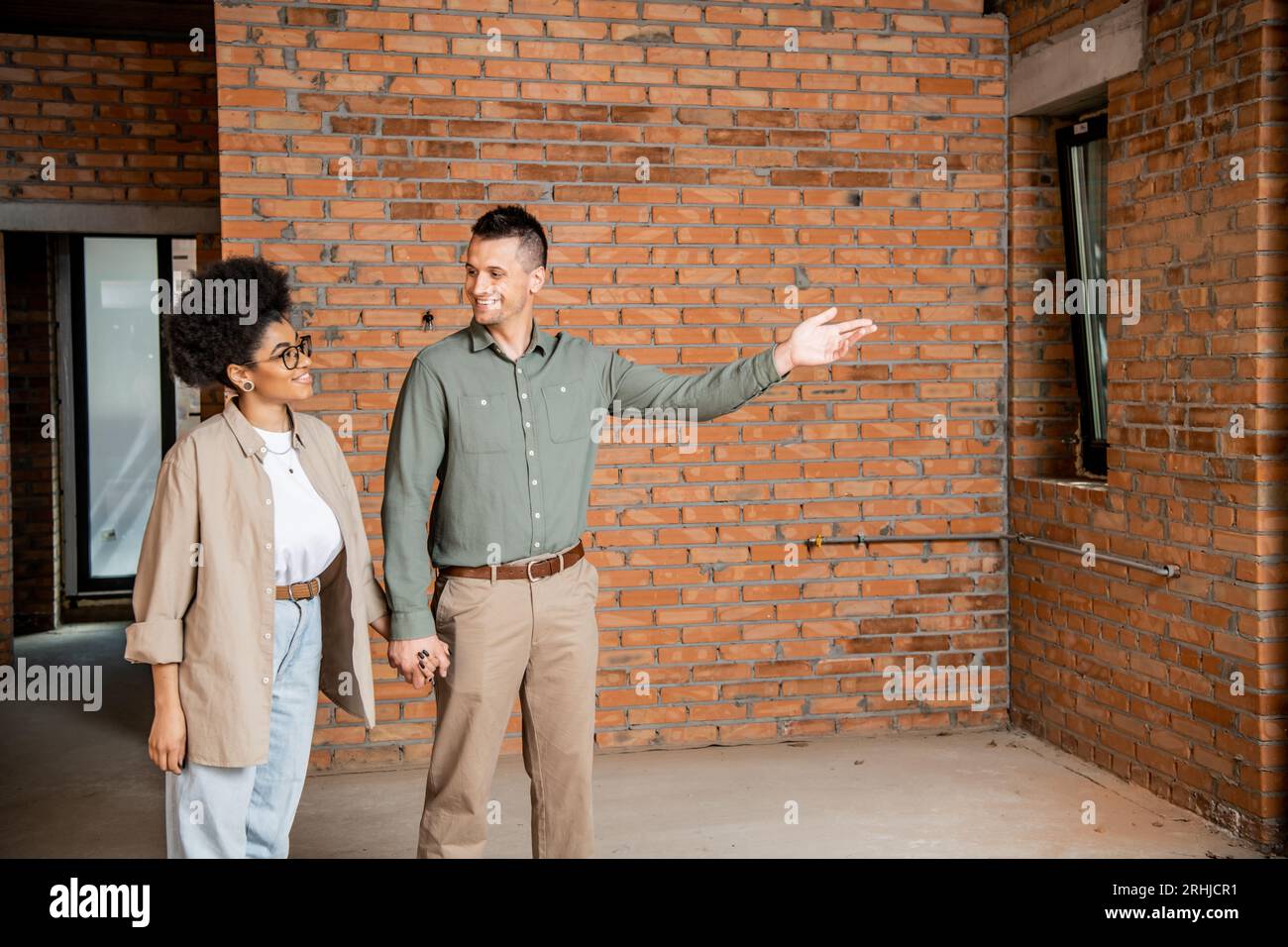 happy man pointing with hand while showing new house to african ...