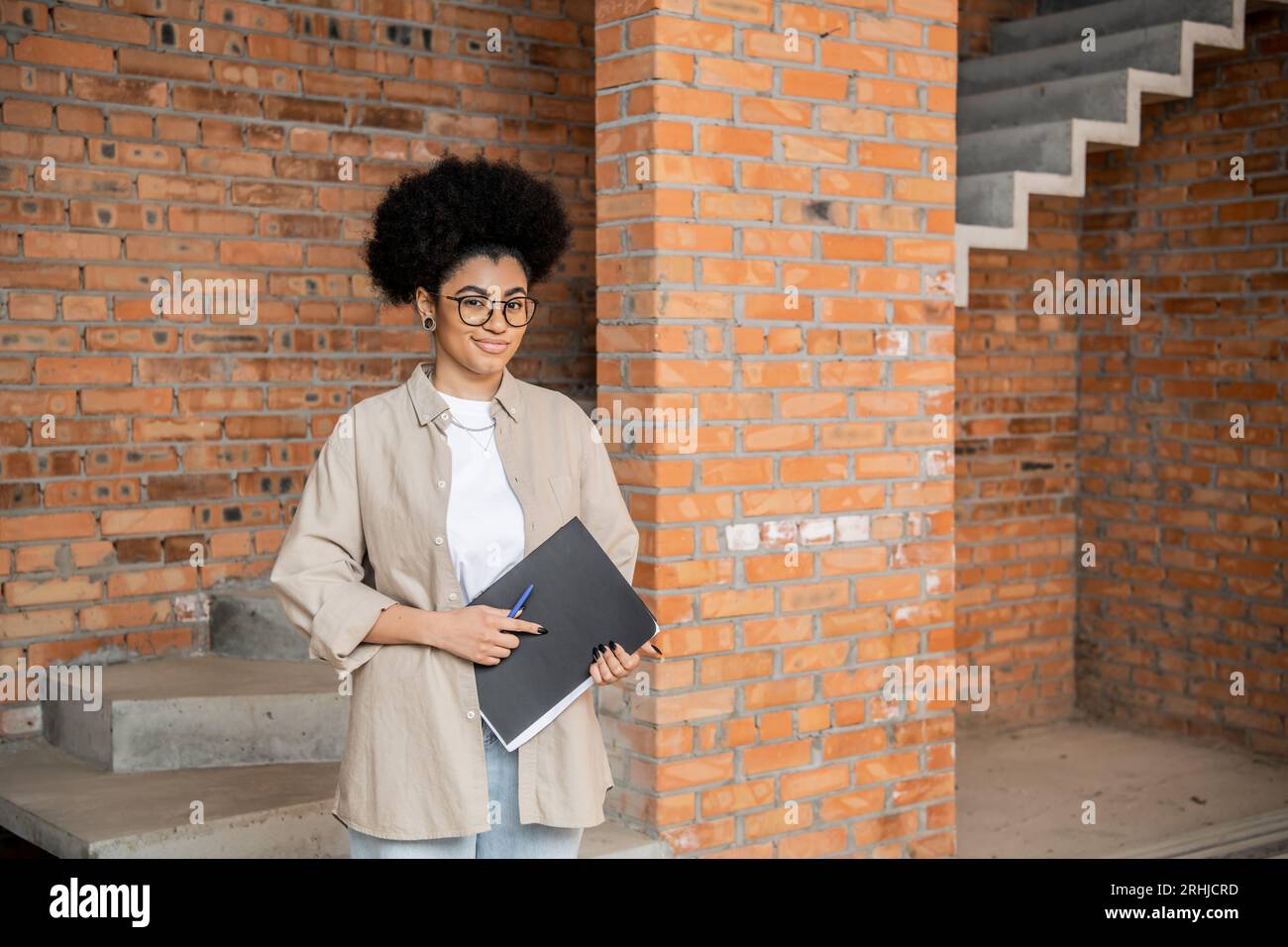 happy african american real estate agent with folder looking at camera ...