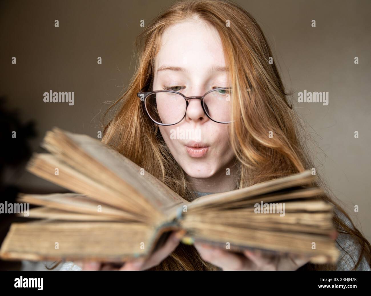 Red-haired beautiful girl with glasses blowing dust off a vintage old ...