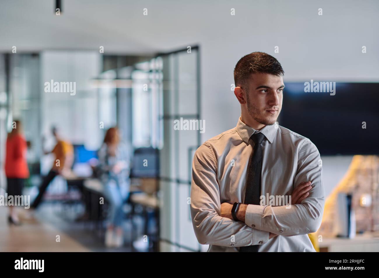 A young business leader stands with crossed arms in a modern office ...
