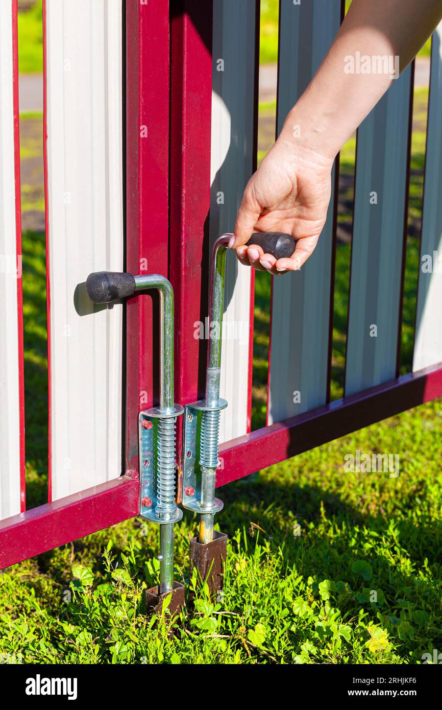 woman opens the bolt on the fence. hand opens the latch on the door ...