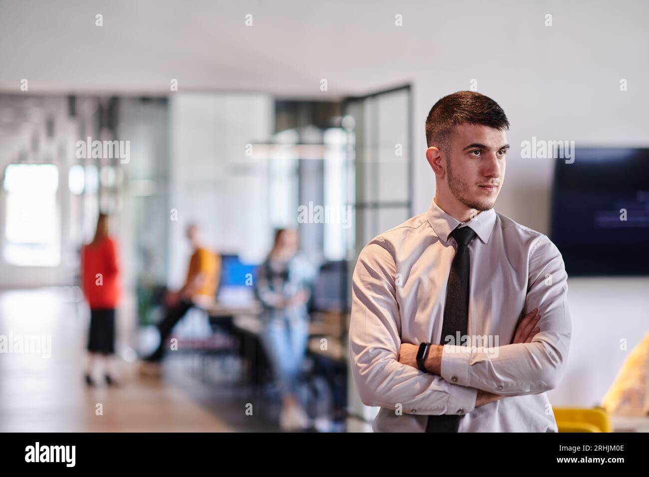A young business leader stands with crossed arms in a modern office ...