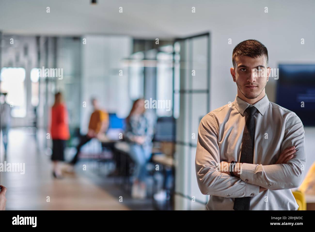 A young business leader stands with crossed arms in a modern office ...
