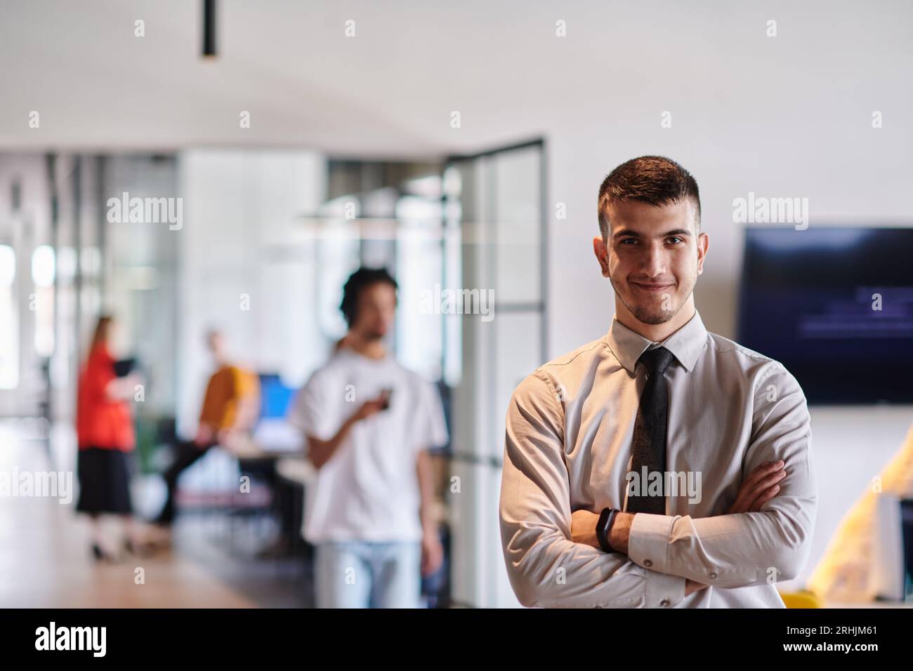 A young business leader stands with crossed arms in a modern office ...