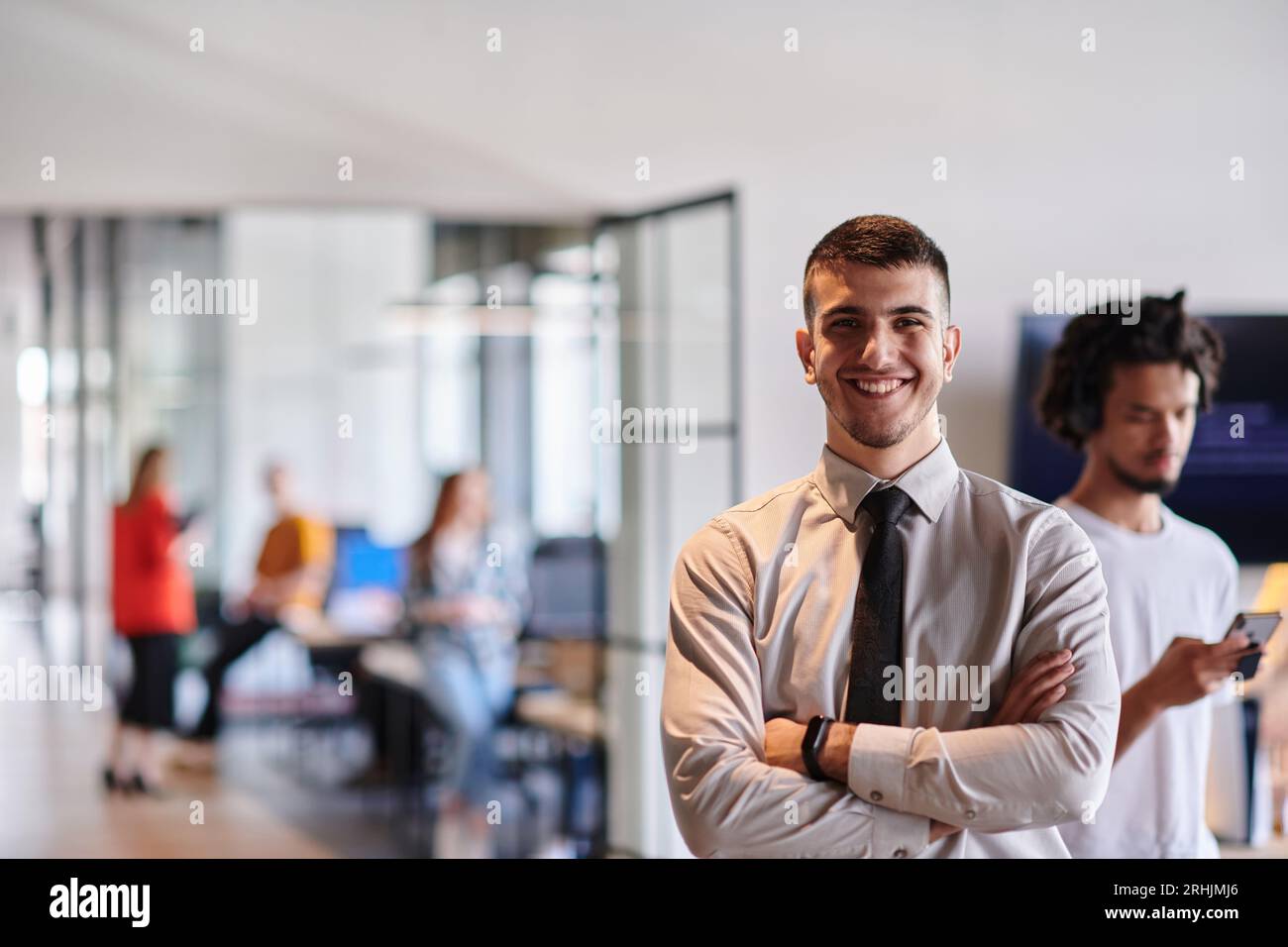 A young business leader stands with crossed arms in a modern office ...