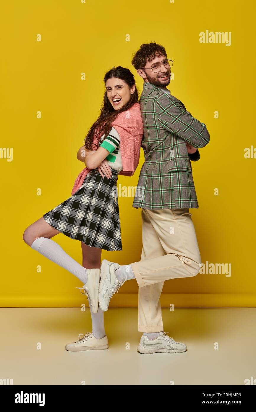happy stylish couple standing back to back, posing on yellow background ...