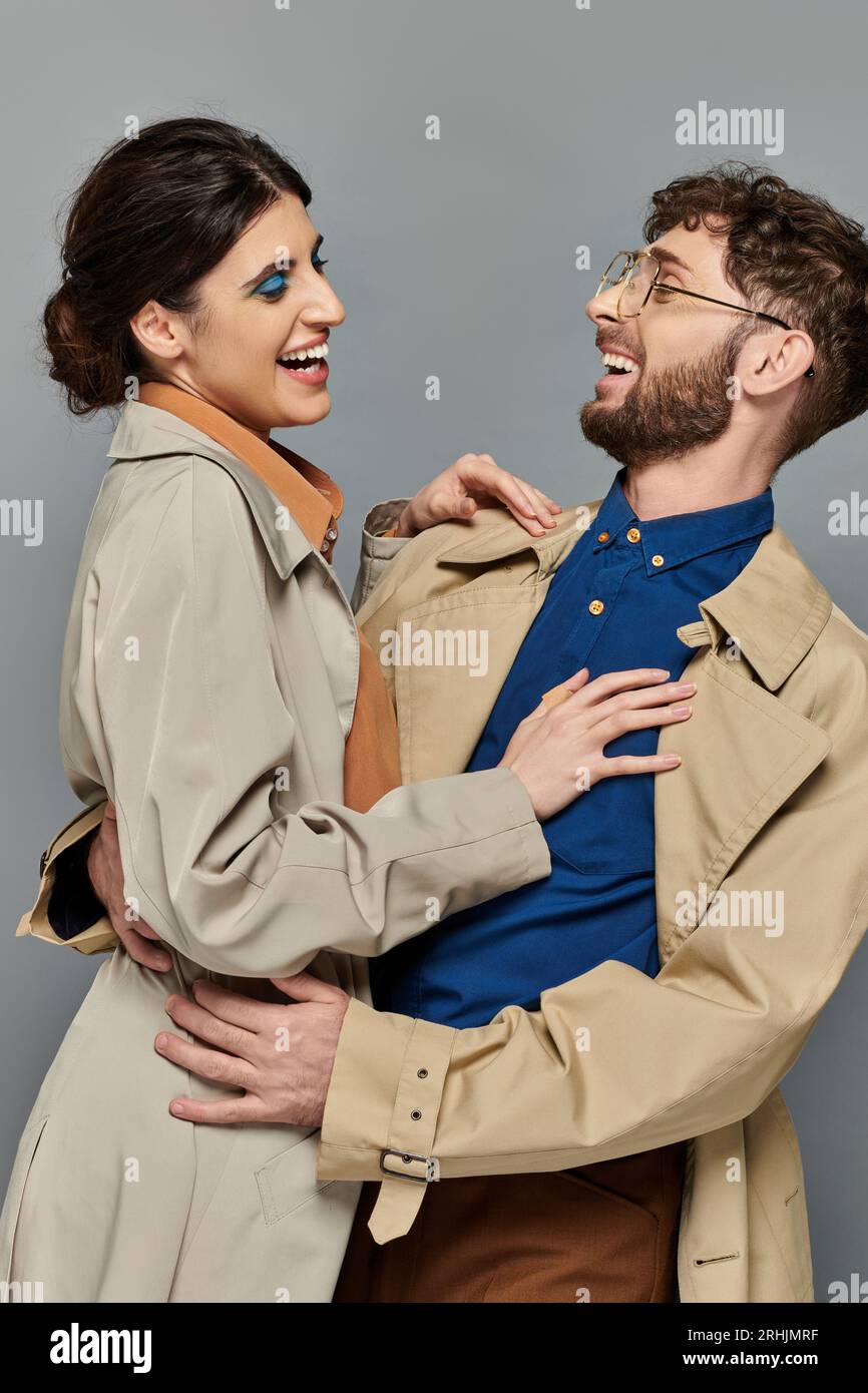 fall season, joyful man and woman hugging on grey background, couple in ...