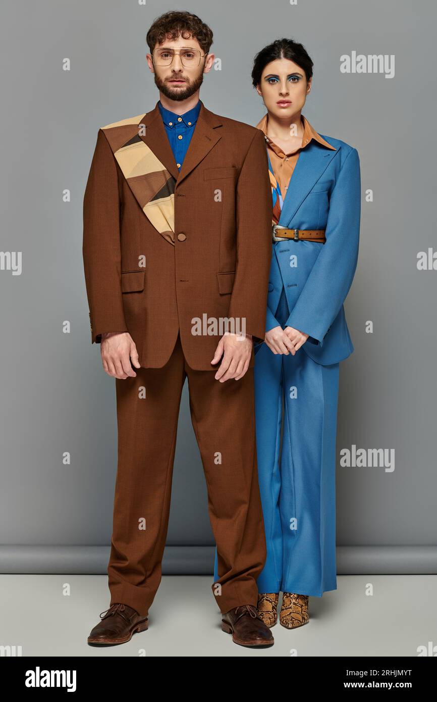 stylish couple posing in tailored suits, formal attire, grey backdrop ...