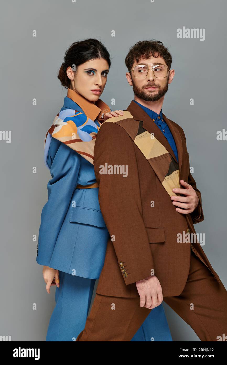 stylish couple in suits posing on grey background, elegant style, bold ...