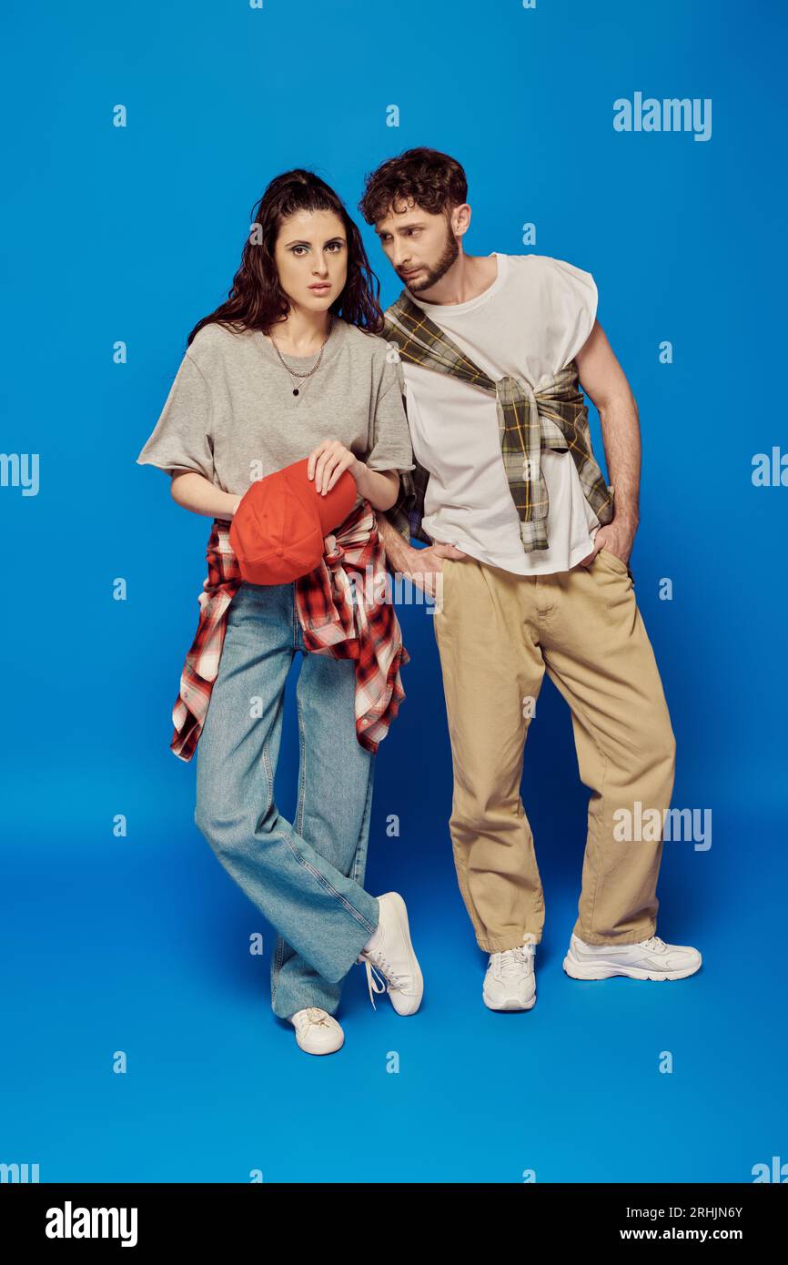 college couple posing in street wear on blue backdrop, woman with bold ...