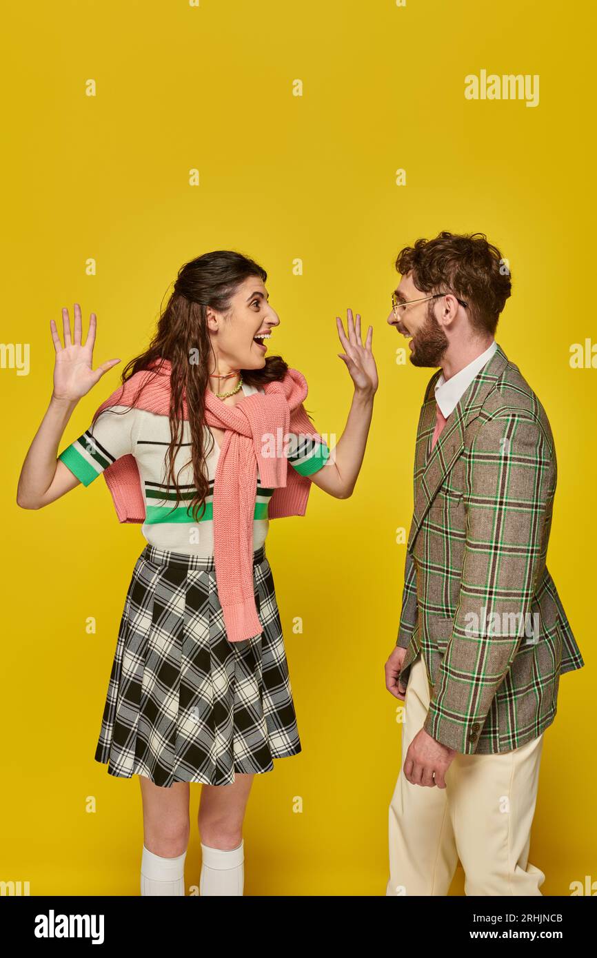 excited woman gesturing and looking at man on yellow backdrop, happy ...