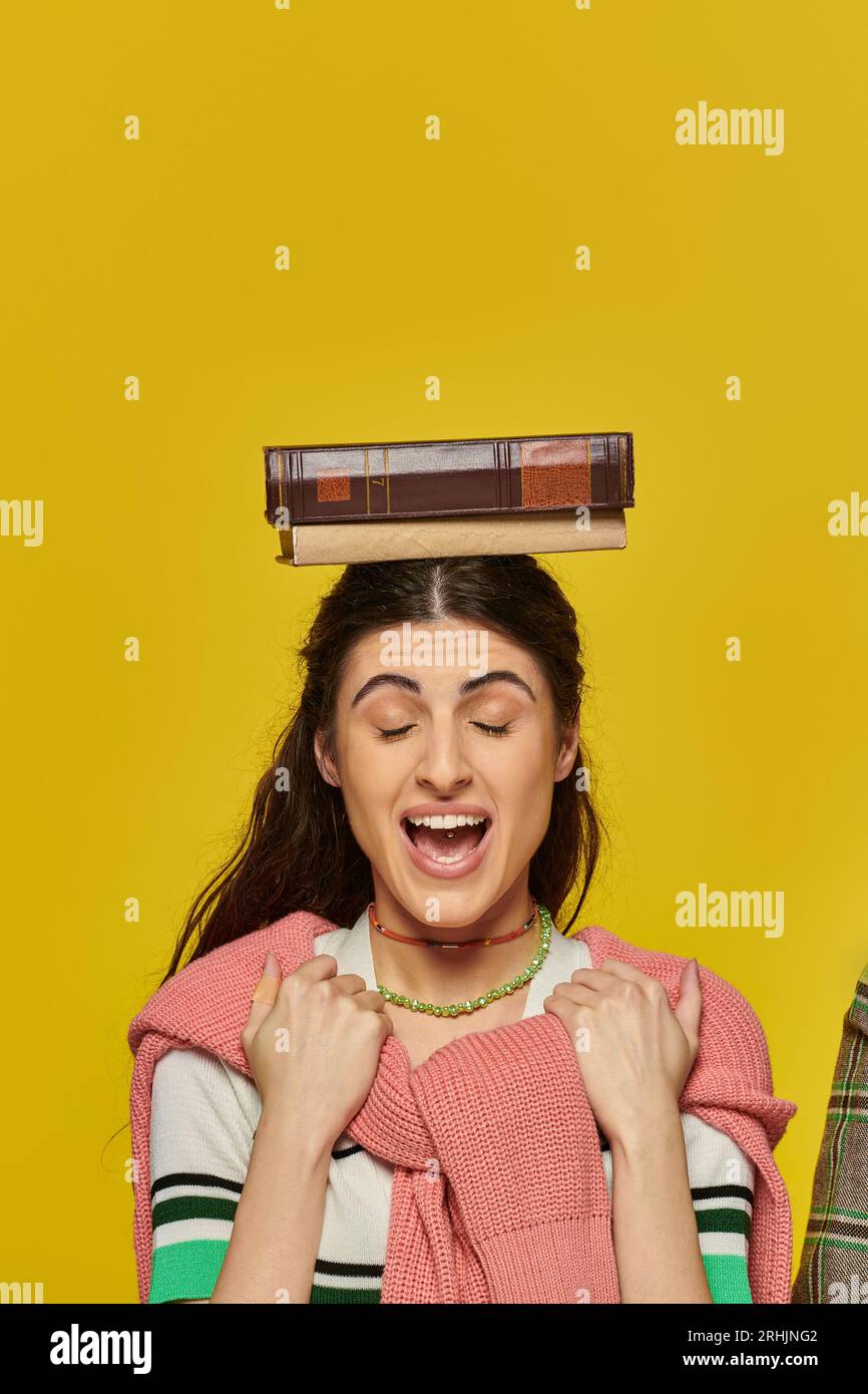 excited woman with closed eyes standing with book on head, yellow ...