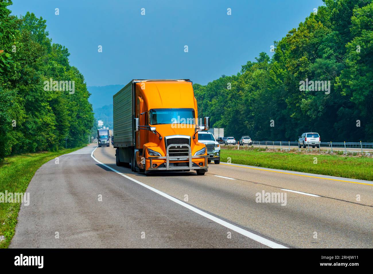 Horizontal shot of an orange eighteen wheeler in traffic on an ...