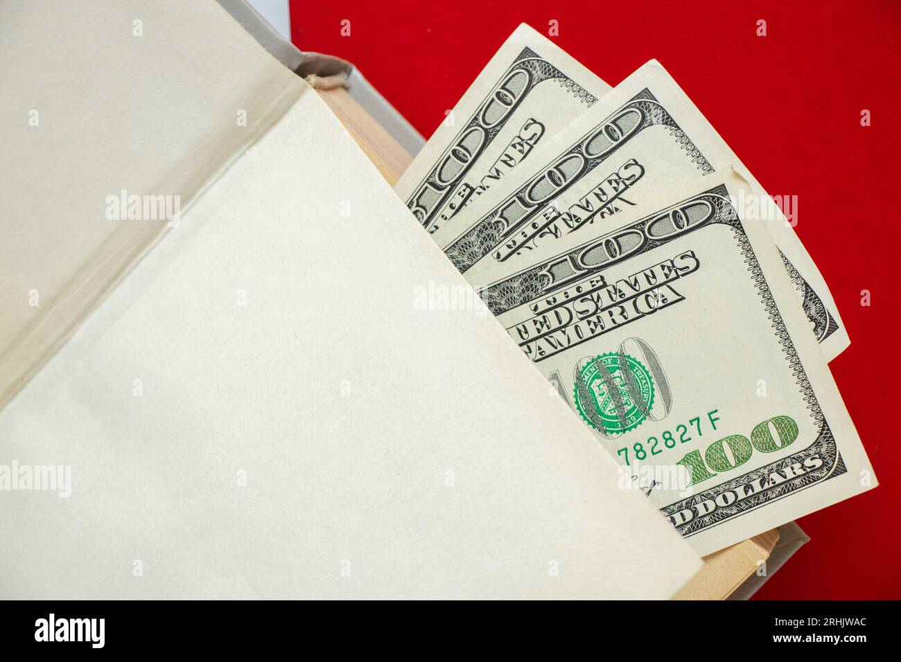 One hundred dollar bills lie in a book against the background of a red ...