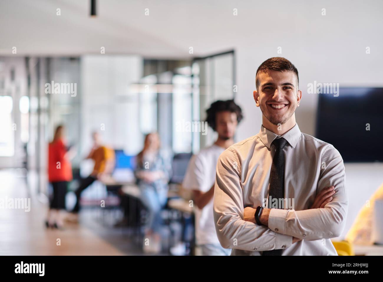 A young business leader stands with crossed arms in a modern office ...