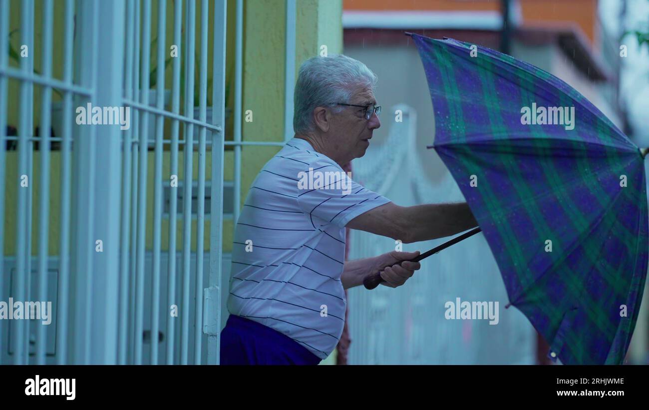 Senior man arriving home during rainy day, holding umbrella and opening ...