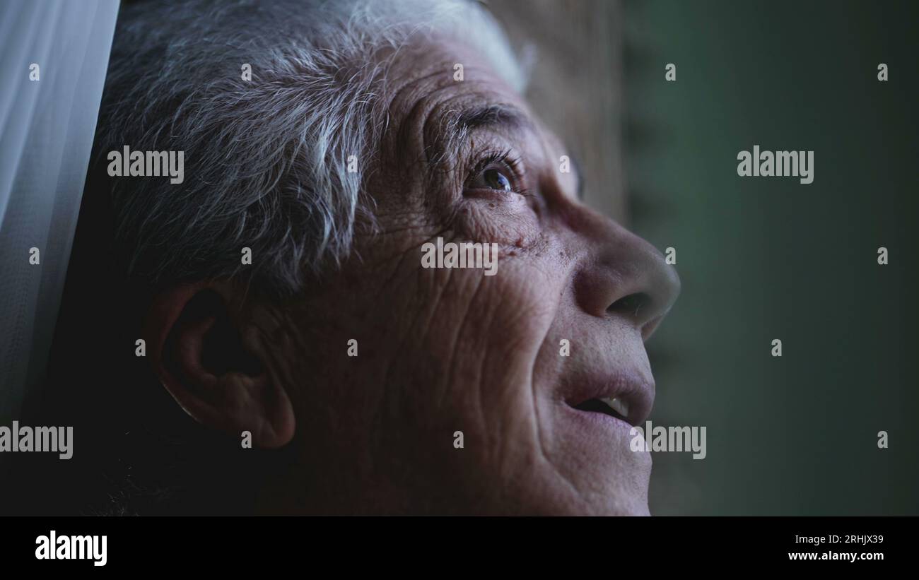Elderly man close-up face looking up at sky from home window, observing ...