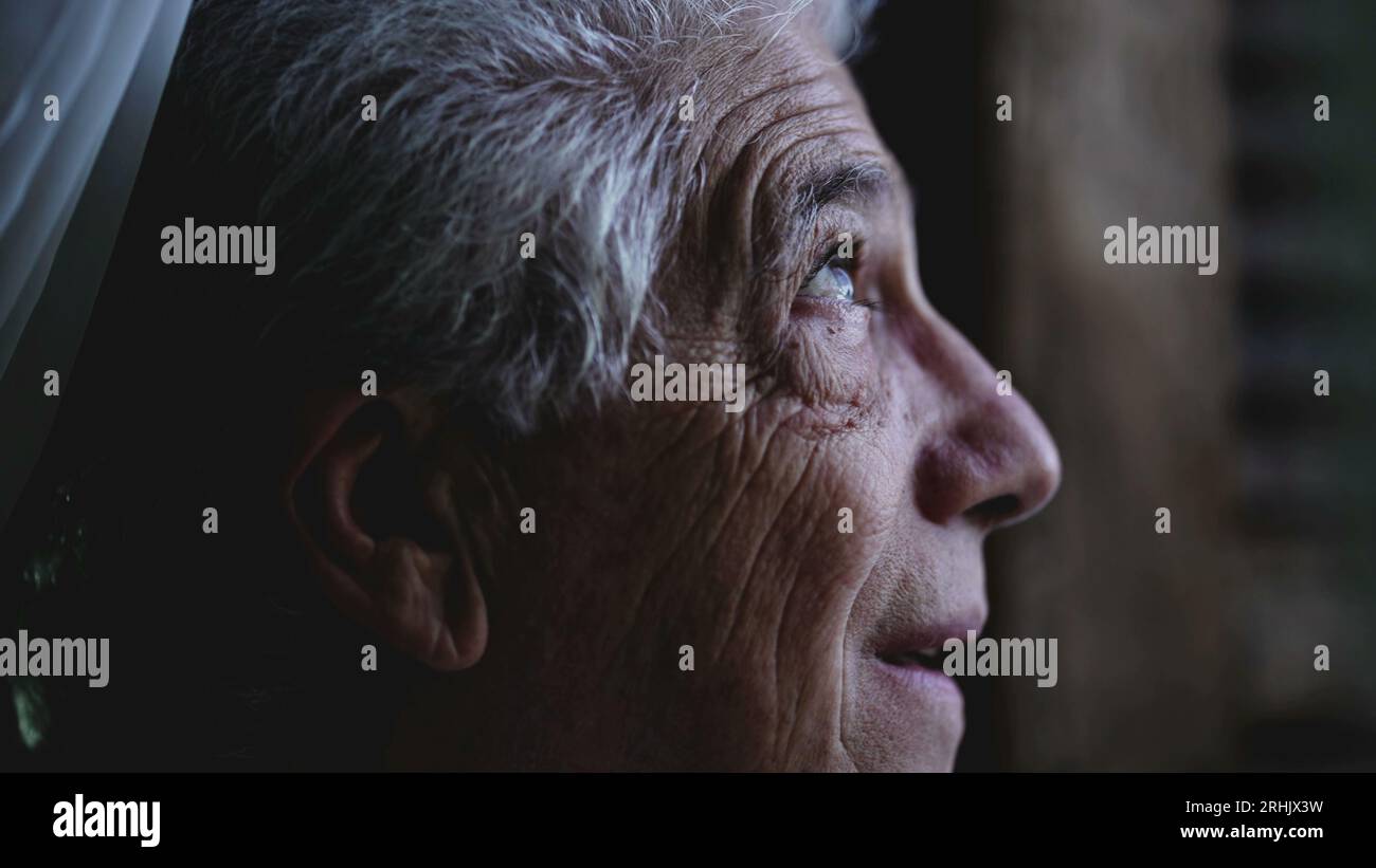 Elderly man close-up face looking up at sky from home window, observing ...