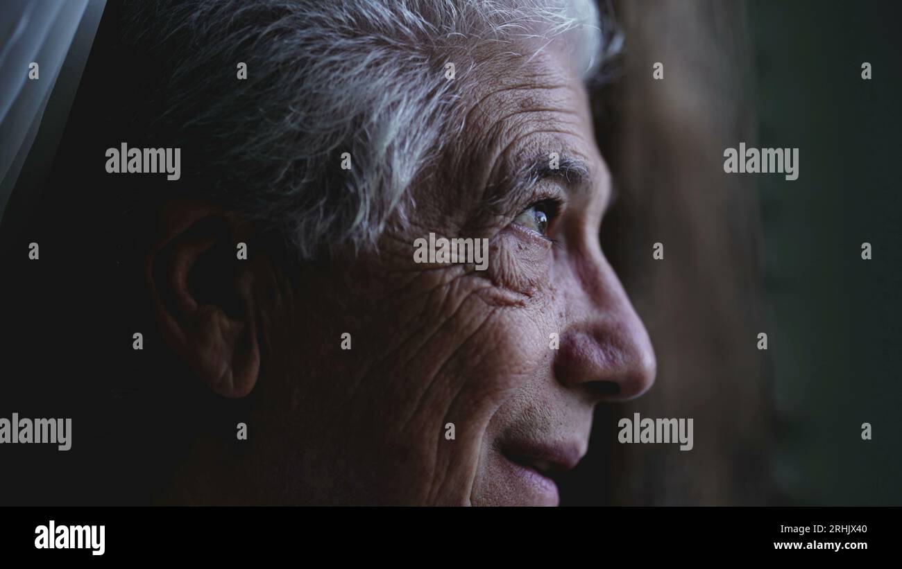 Elderly man close-up face looking up at sky from home window, observing ...