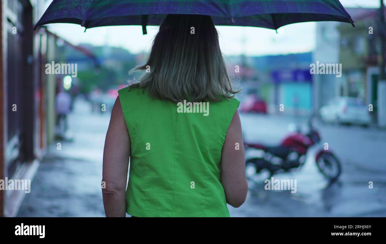 Back of person walking in the rain holding umbrella. Woman strolling in ...