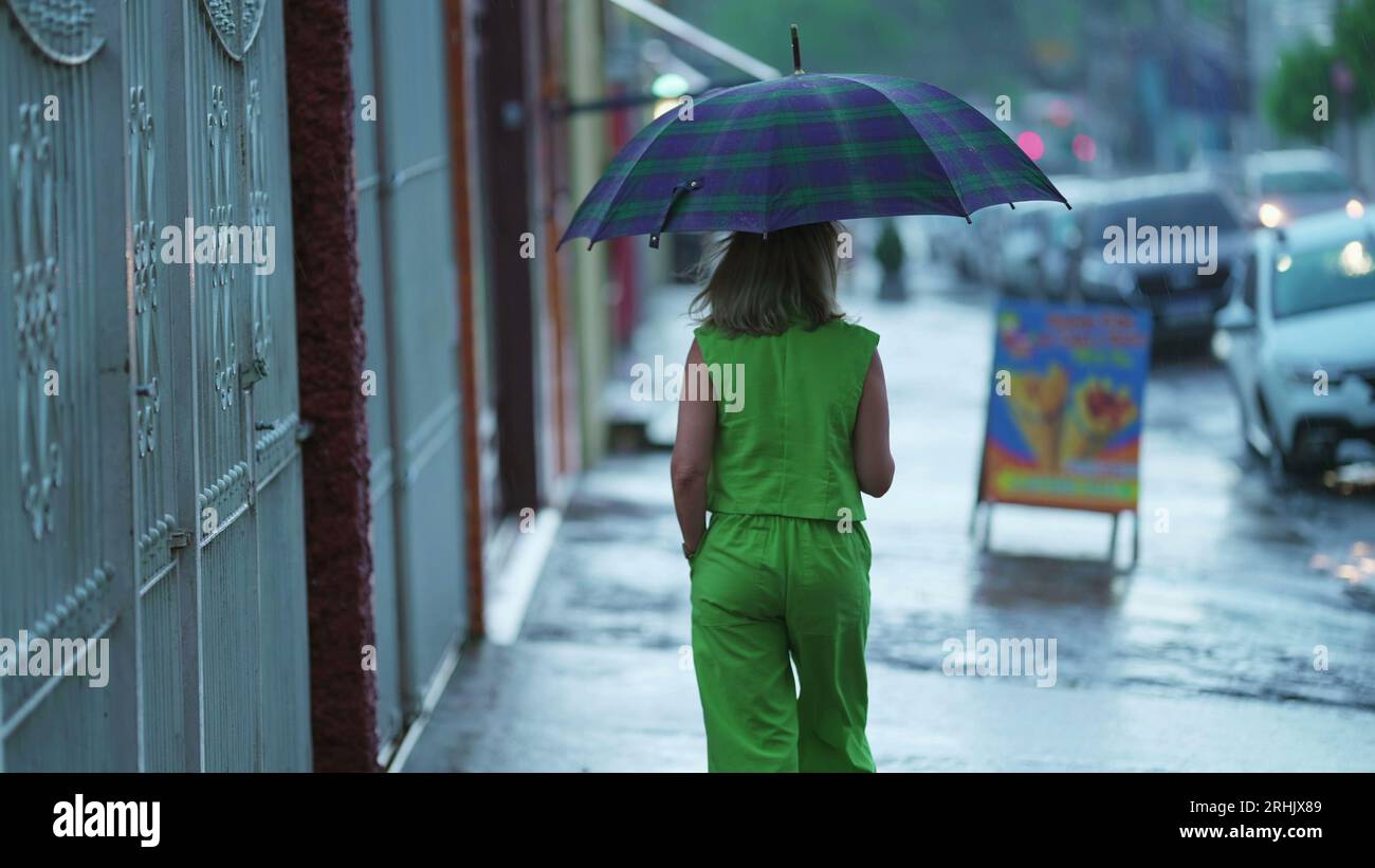 Back of woman walking in the rain holding umbrella. Person strolling ...
