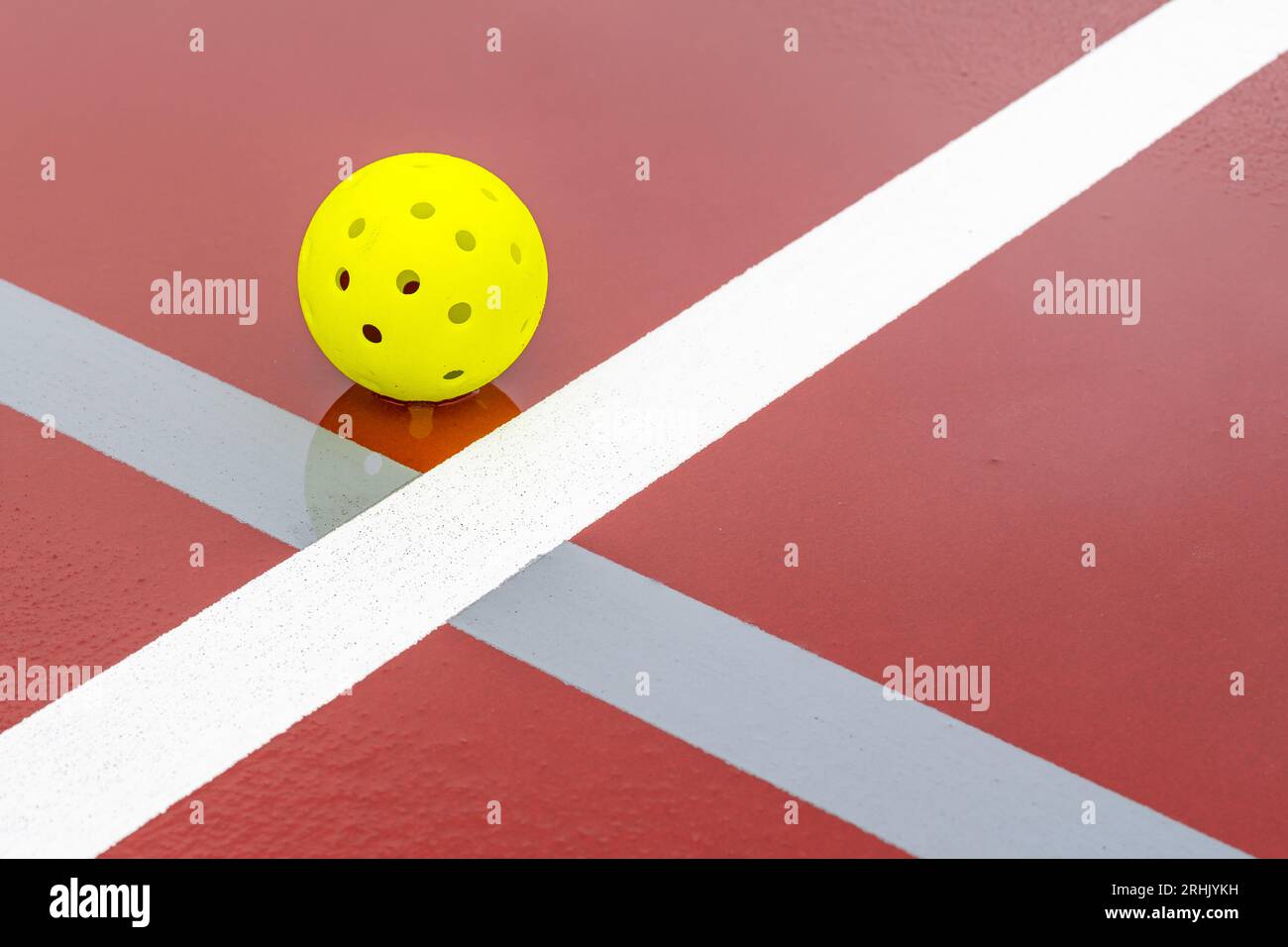 A pickleball on a wet red pickleball tennis court with white lines ...