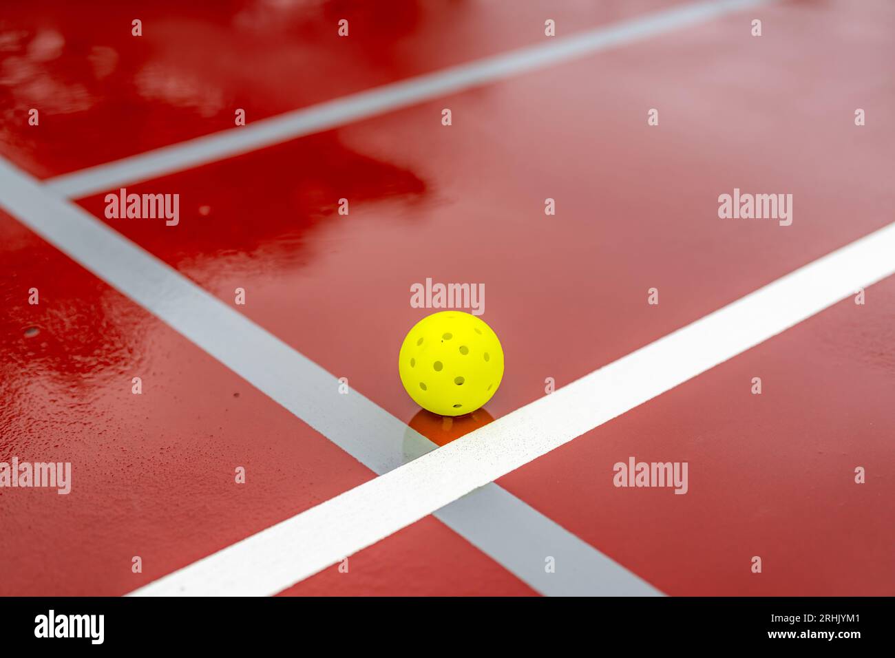 A pickleball on a wet red pickleball tennis court with white lines ...