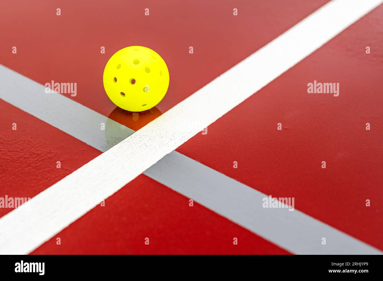 A pickleball on a wet red pickleball tennis court with white lines ...
