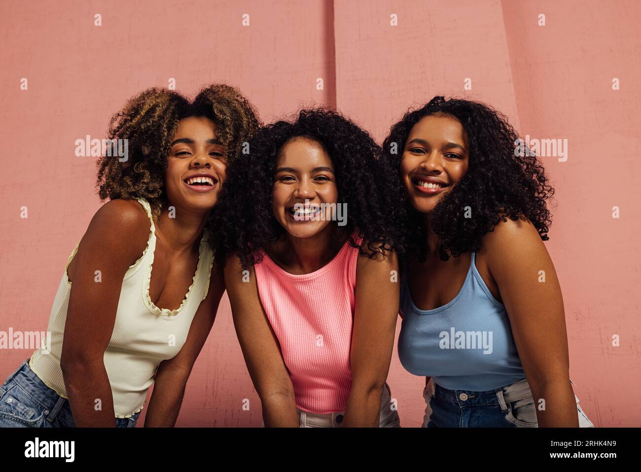 Three happy girls with curly hair standing together and looking at ...
