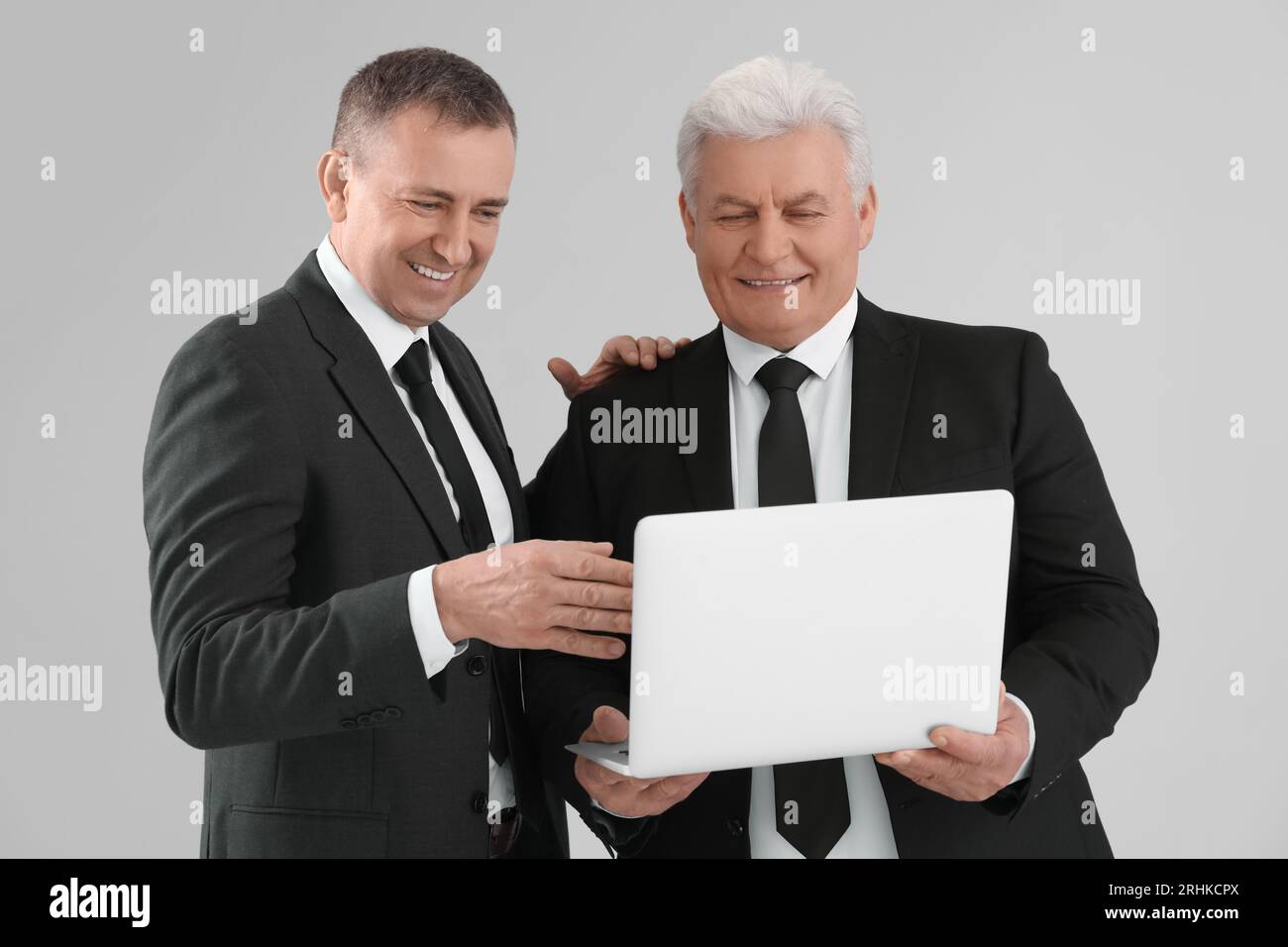 Mature brothers in suits using laptop on grey background Stock Photo ...