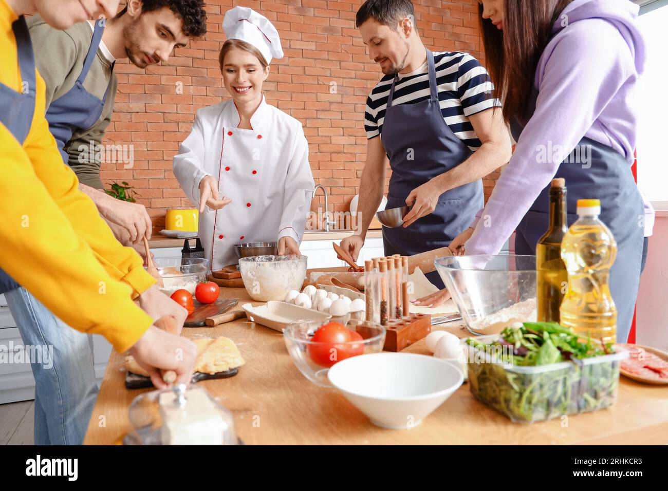 Group of young people with chef preparing Italian pizza during cooking ...