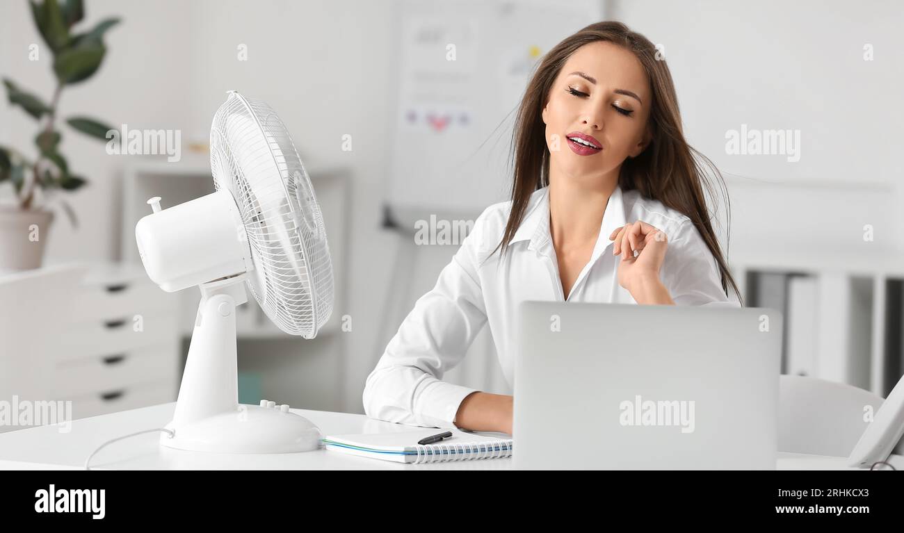 Young woman using electric fan during heatwave in office Stock Photo ...