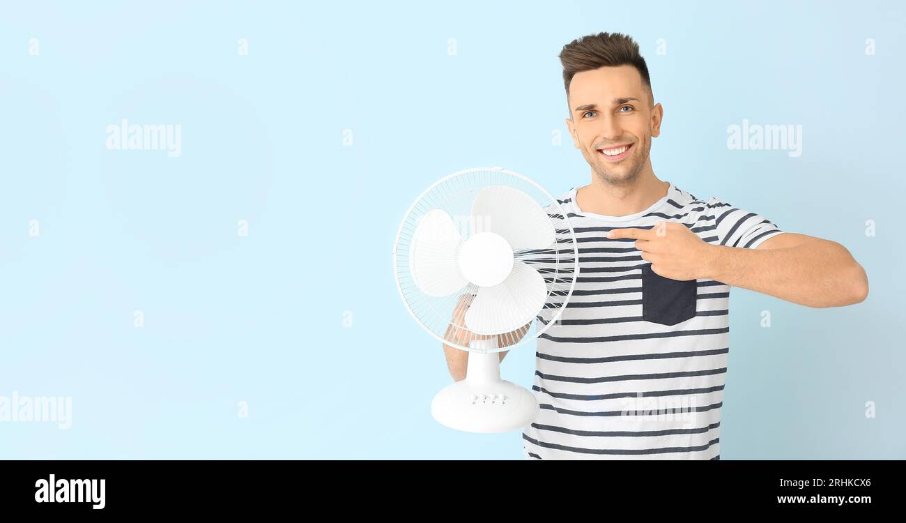 Young man with electric fan on light blue background. Banner for design ...