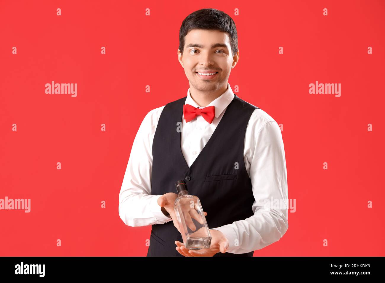Male waiter with bottle of vodka on red background Stock Photo - Alamy