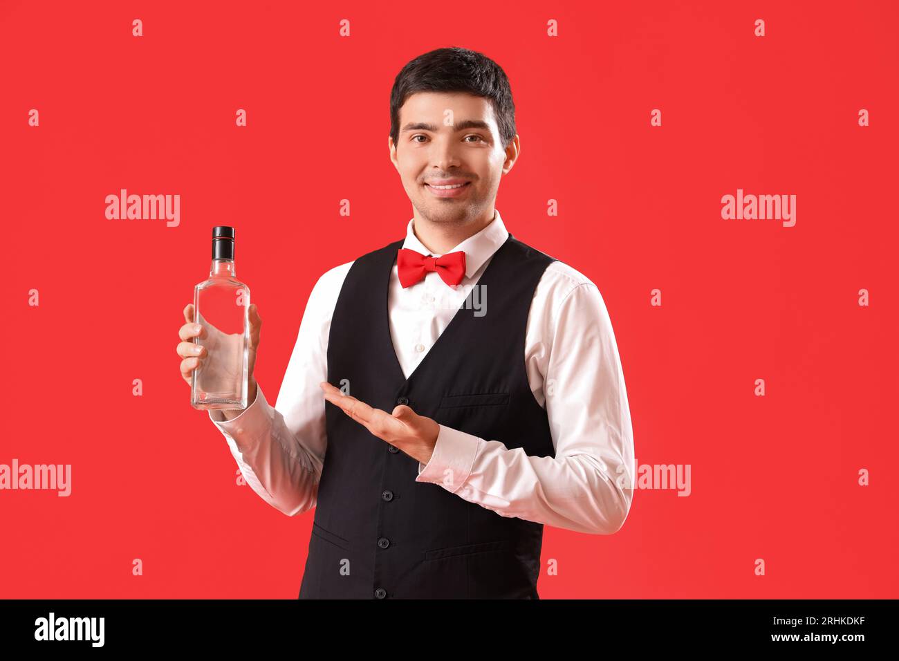 Male waiter with bottle of vodka on red background Stock Photo - Alamy