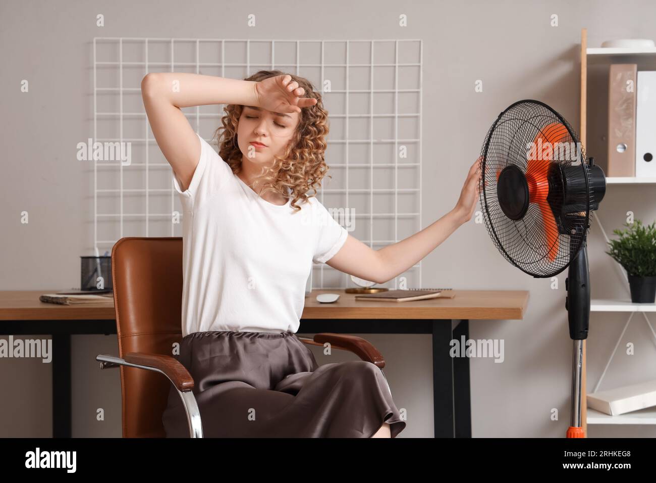 Beautiful young woman with electric fan sitting on chair at home during heatwave Stock Photo - Alamy