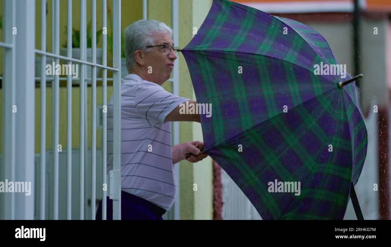 Senior man opening umbrella, steps out to street in the rain, closes ...