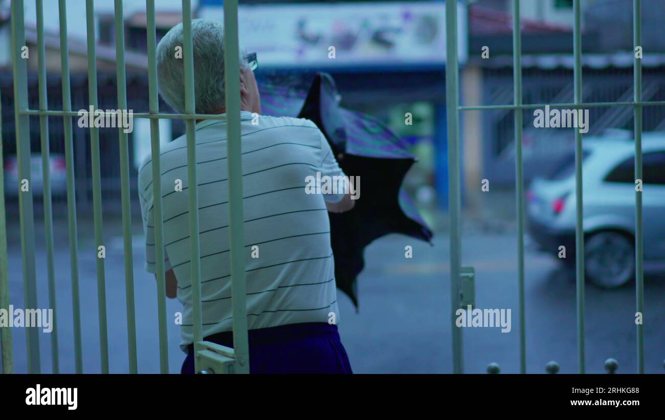 Senior man stepping out in the street during rainy evening, opening ...