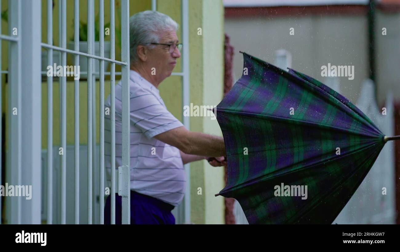 Senior man opening umbrella, steps out to street in the rain, closes ...